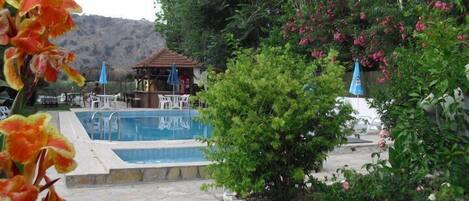 Área de piscina com um pequeno gazebo, rodeada por vegetação exuberante e plantas floridas.