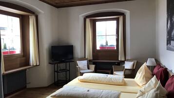 Quarto de hotel com duas camas, televisão e janelas amplas com cortinas.