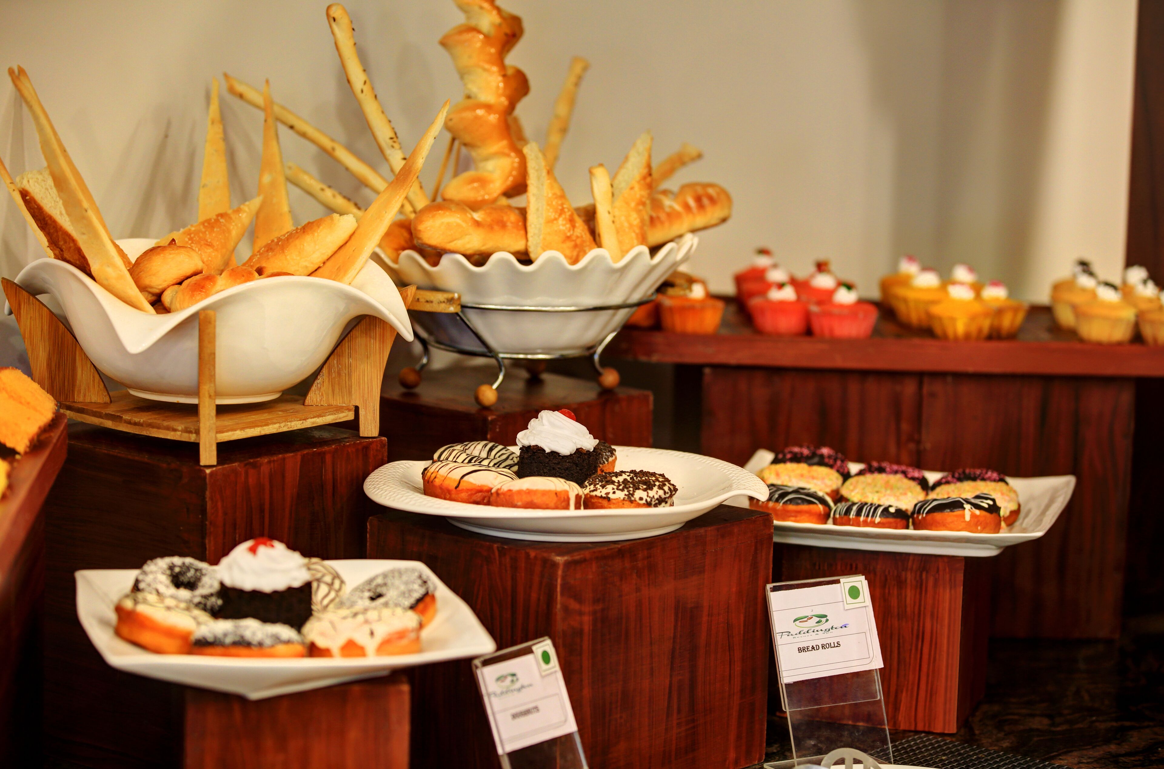 Buffet com diversos produtos de panificação, incluindo pães, doces e donuts.