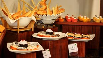 Buffet com diversos produtos de panificação, incluindo pães, doces e donuts.