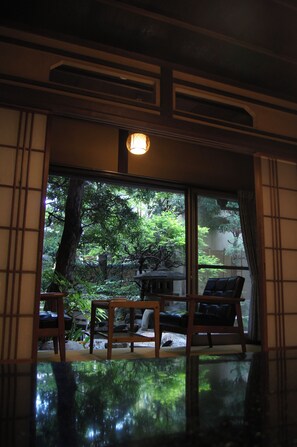 Um quarto japonês tradicional com tatames, uma mesa baixa e vista para um jardim exuberante através de grandes portas deslizantes.