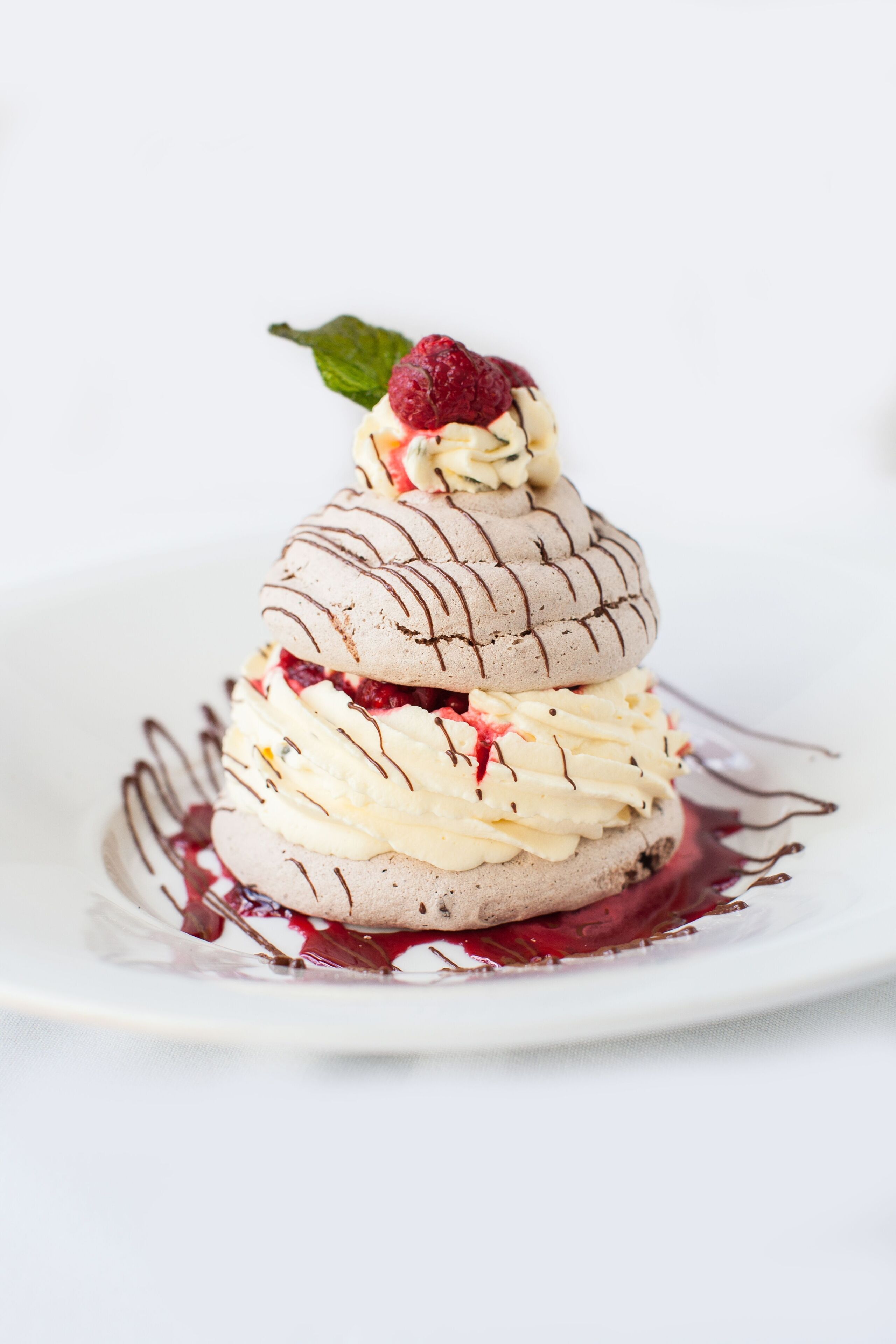 Uma sobremesa com camadas de merengue e creme, coberta com framboesa e folha de hortelã.