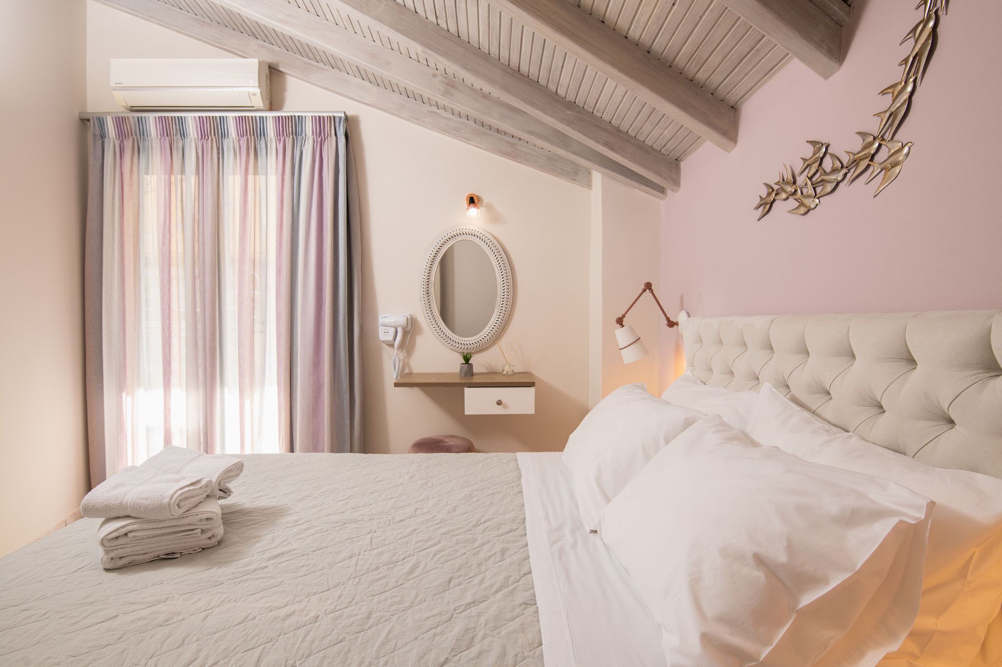 Quarto de hotel com cama, mesa de cabeceira com espelho, luminária pendente e janela com cortinas.