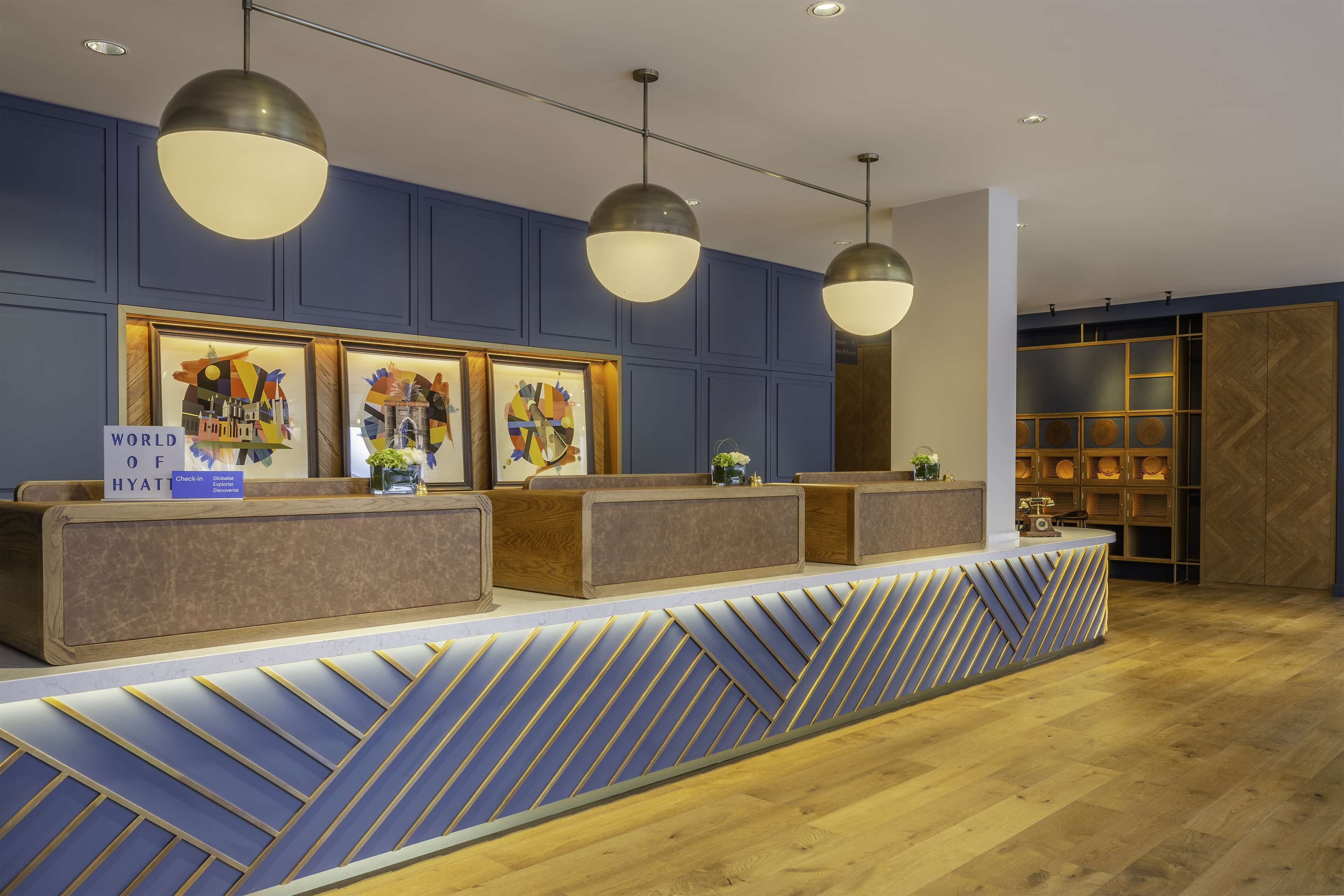 Uma área de recepção de hotel com design moderno, apresentando um balcão de atendimento, obras de arte emolduradas e um balcão de check-in.