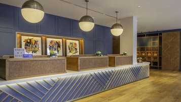 Uma área de recepção de hotel com design moderno, apresentando um balcão de atendimento, obras de arte emolduradas e um balcão de check-in.