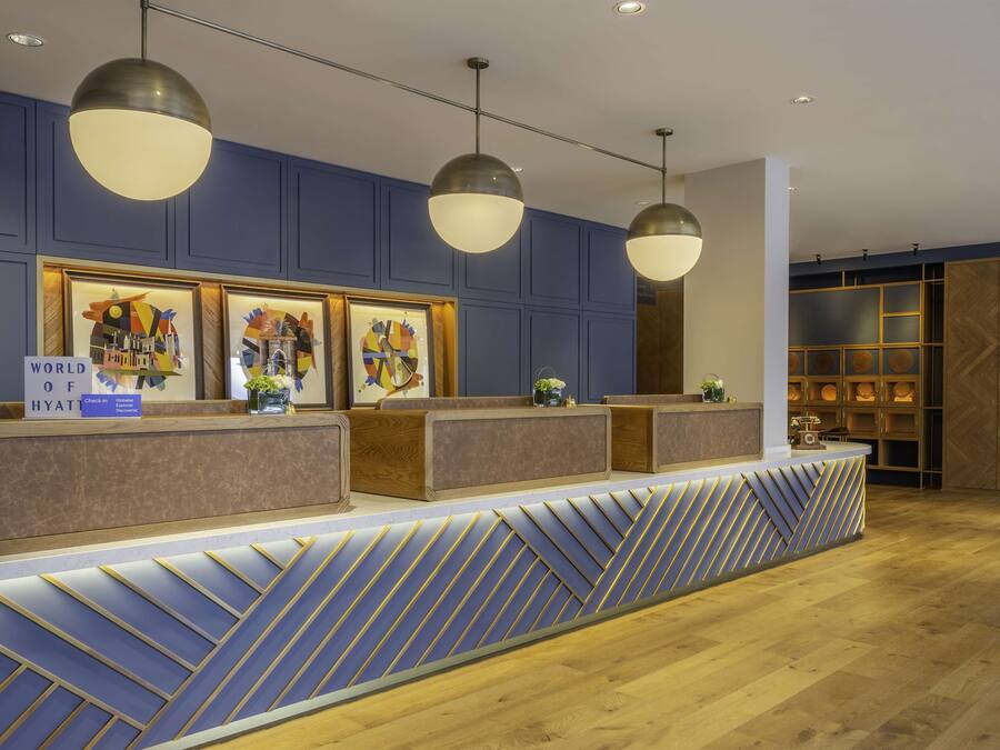 Uma área de recepção de hotel com design moderno, apresentando um balcão de atendimento, obras de arte emolduradas e um balcão de check-in.