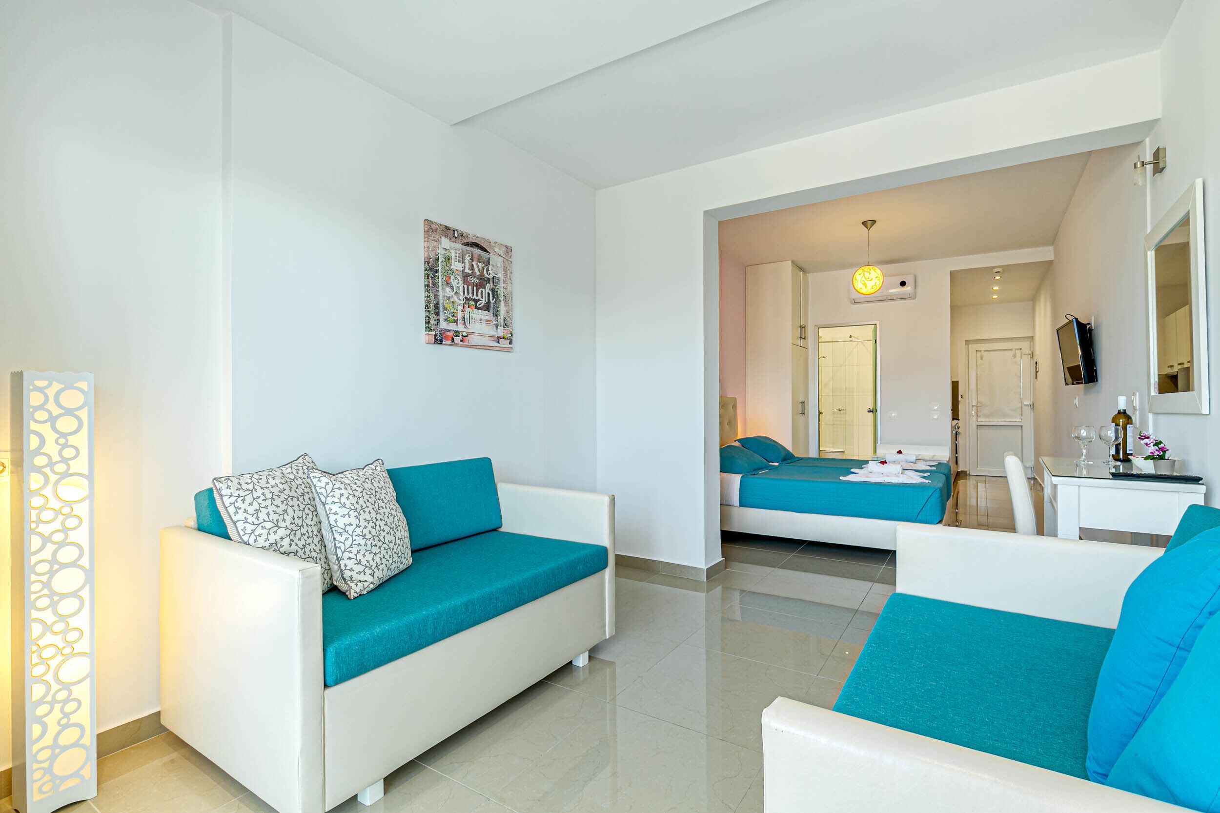 Quarto de hotel moderno com esquema de cores branco e verde-água, apresentando um sofá, uma cama e uma escrivaninha com uma cadeira.