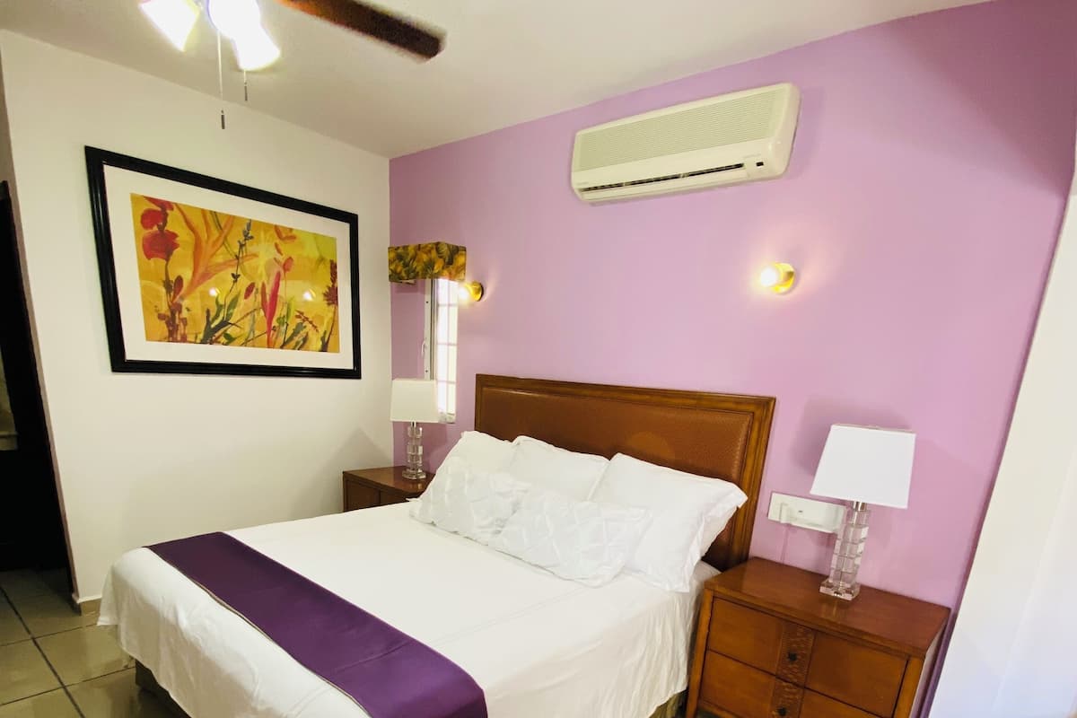 Quarto com cama, mesas de cabeceira, ventilador de teto, ar condicionado e luminária na parede.