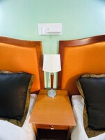 Quarto de hotel com duas camas, uma mesa de cabeceira de madeira com abajur e um aparelho de ar condicionado na parede.