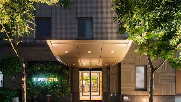 Entrada de hotel com design moderno, com porta de vidro e letreiro luminoso.