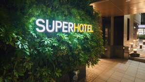 Entrada de um hotel com uma placa que diz "SUPERHOTEL" iluminada por luzes.