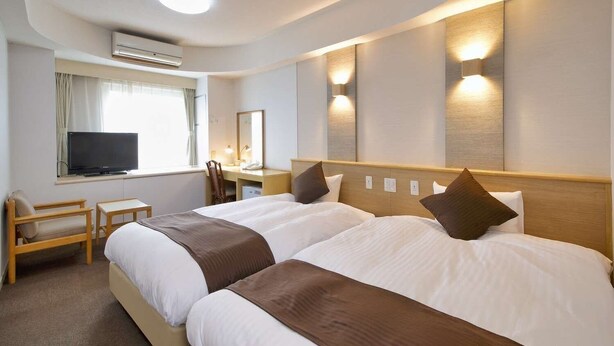 Quarto de hotel com duas camas, uma escrivaninha, uma cadeira, uma televisão e uma janela grande.