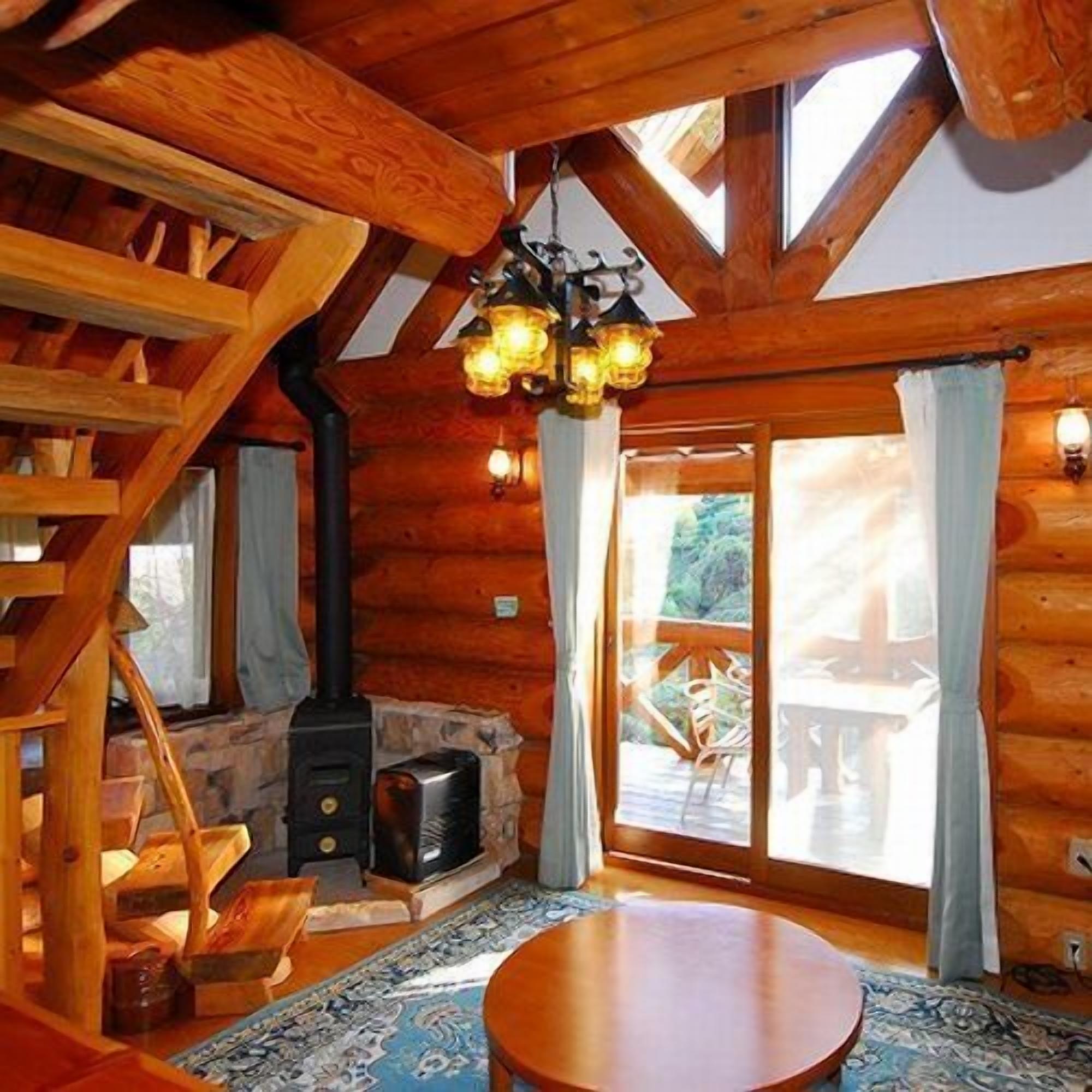 Interior de uma cabana de tronco com lareira, escada de madeira e janelas amplas.