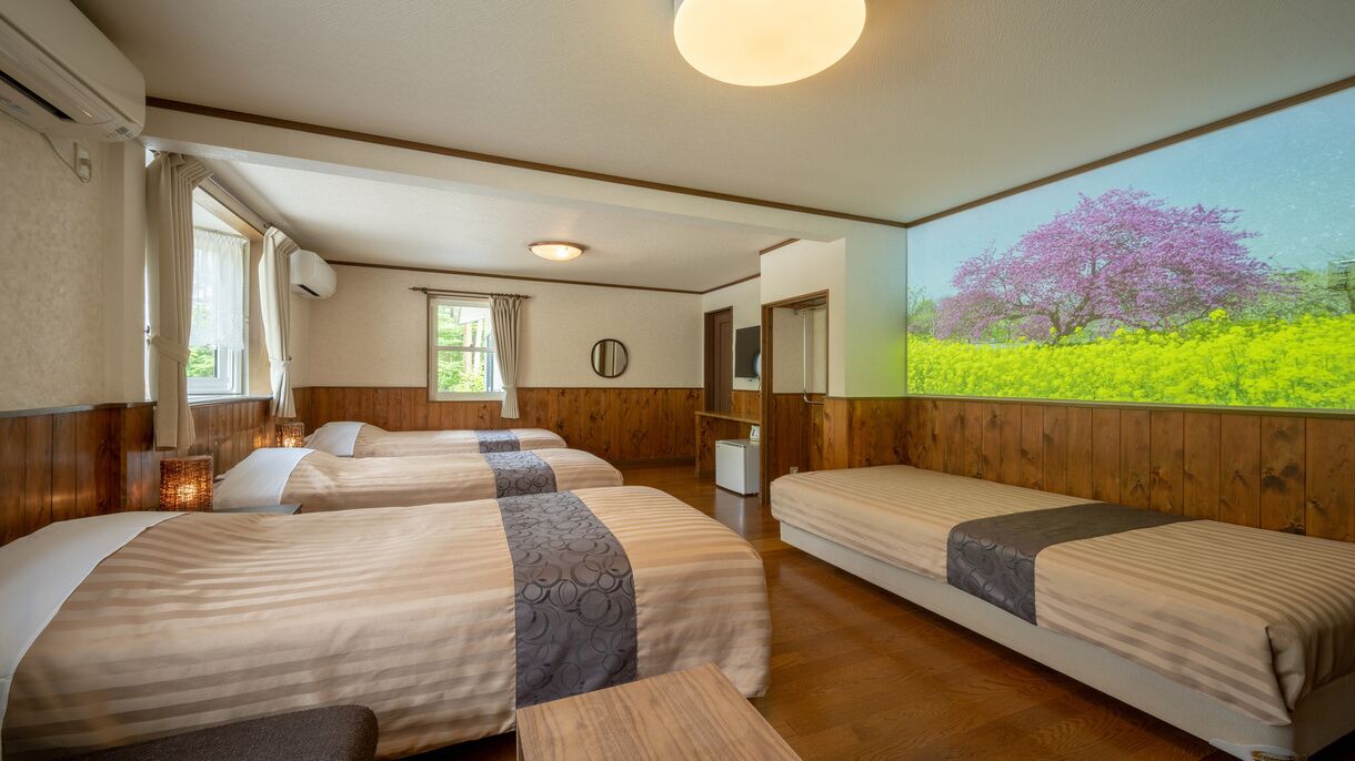 Quarto de hotel com duas camas, piso de madeira, uma janela grande com cortinas, televisão presa na parede e um quadro de uma árvore.