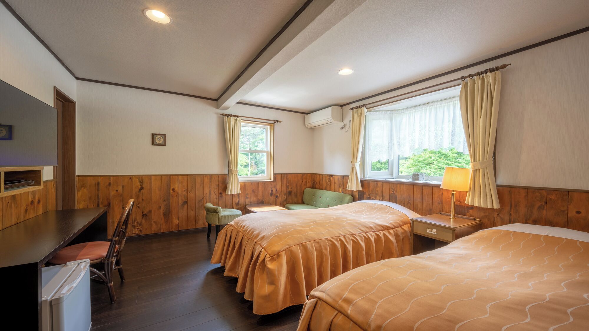 Quarto de hotel com duas camas, uma escrivaninha, uma cadeira e janela com cortinas.