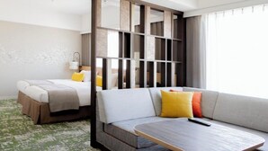 Quarto de hotel com cama, sofá, uma mesa pequena e um divisória.