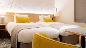 Quarto de hotel com duas camas, uma mesinha e uma cadeira.