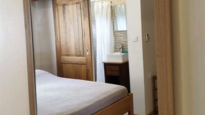 Quarto com cama, guarda-roupa de madeira e banheiro visível através de um espelho.