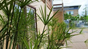 Varanda com vasos de plantas e vista para um edifício com piso de azulejos e grade de metal.