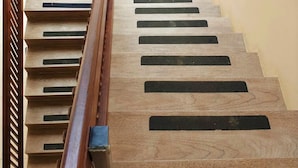Escadaria de madeira com corrimão de metal, que leva a um patamar com piso estampado.