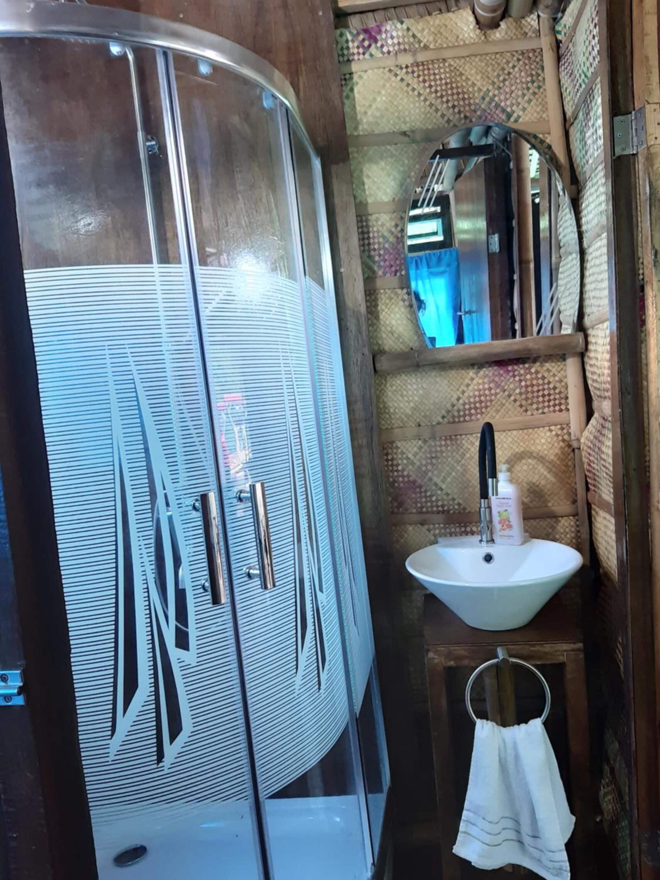 Casa de banho com cabine de chuveiro em vidro, lavatório branco e um pequeno porta-toalhas.