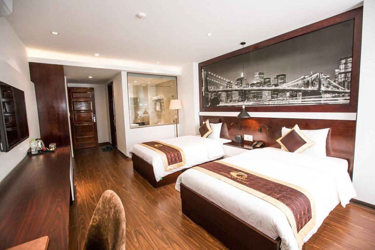Quarto de hotel com duas camas, uma grande pintura de paisagem urbana, uma escrivaninha e uma cadeira.