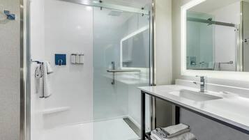 Uma casa de banho moderna com cabine de duche em vidro, um espelho grande e lavatório branco.