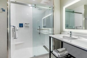 Uma casa de banho moderna com cabine de duche em vidro, um espelho grande e lavatório branco.
