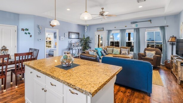 Uma sala de estar ampla com um sofá azul, uma mesa de jantar com cadeiras e uma ilha de cozinha com bancada de granito.