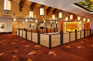 Um hall de hotel com carpete estampado em padrão geométrico, balcão de recepção e várias luminárias pendentes em estilo de lanterna.
