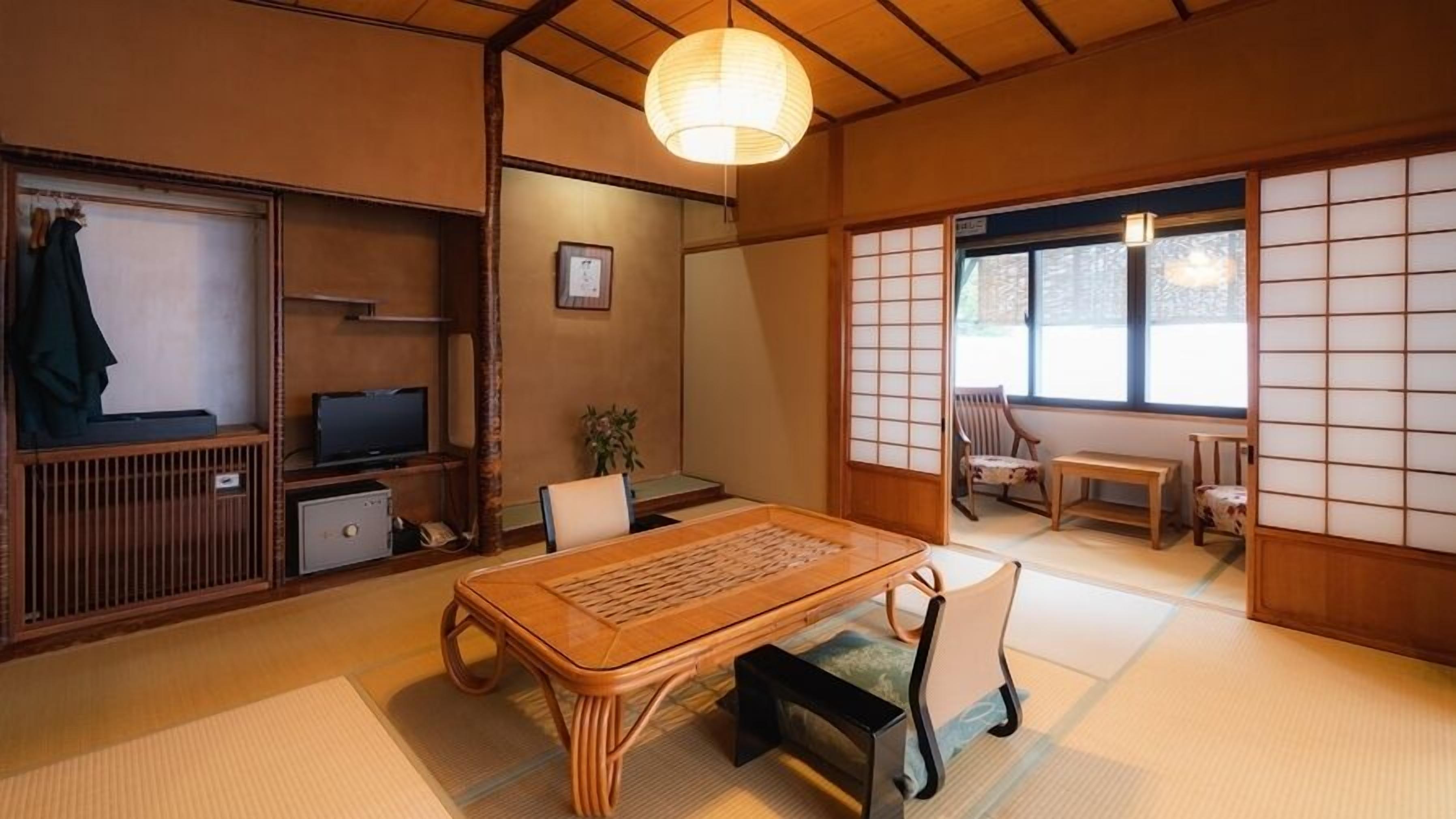 Um quarto japonês tradicional com piso de tatame, uma mesa baixa, cadeiras, uma televisão e portas deslizantes.