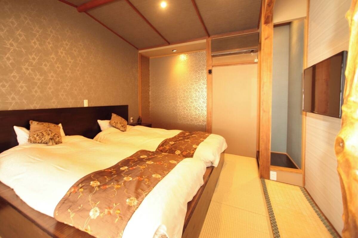 Quarto de hotel com uma cama grande, mesa de cabeceira, cabeceira de madeira e parede com padrão geométrico.