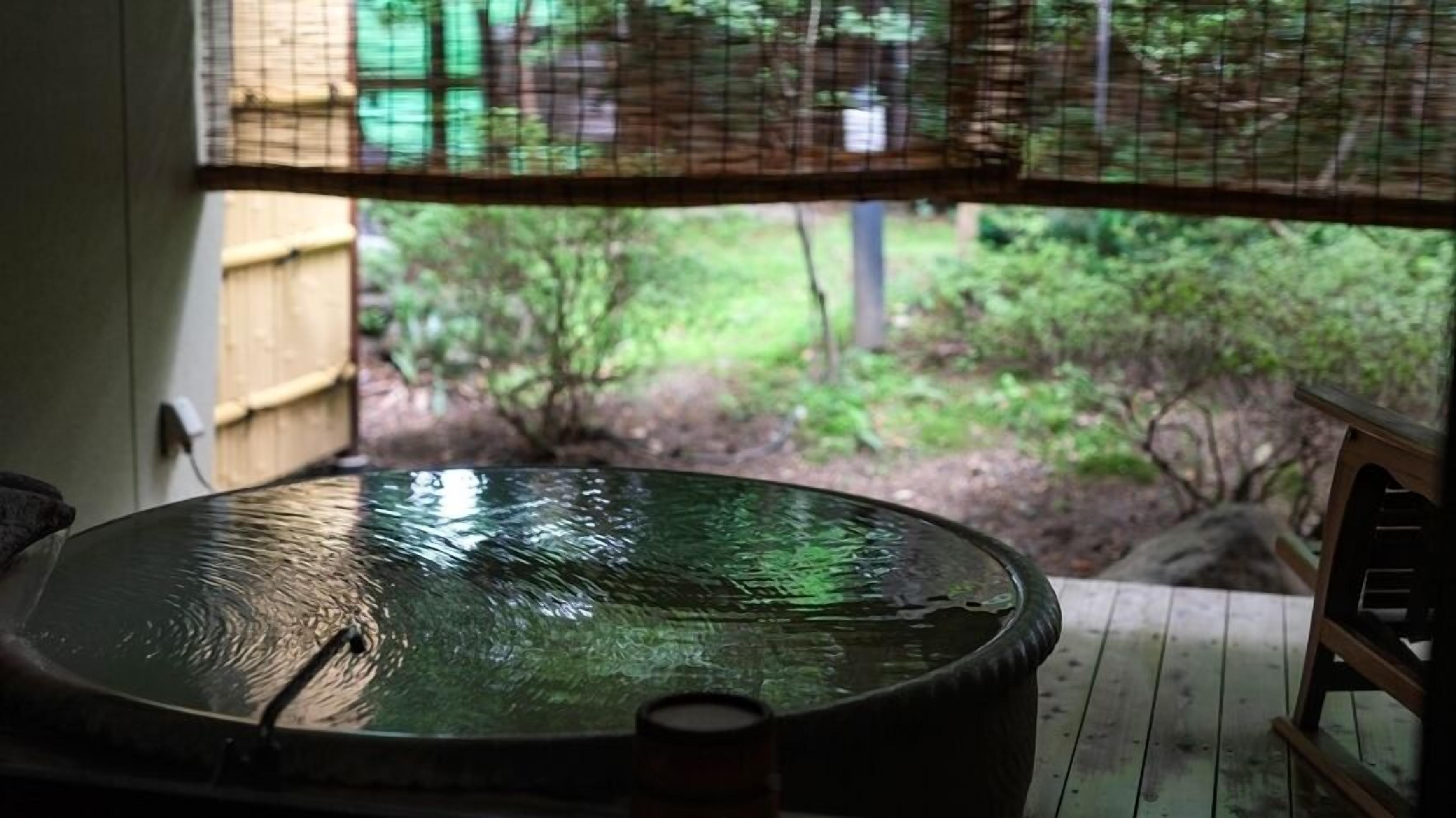 Mesa redonda com superfície refletora, uma cadeira e vista para um jardim através de uma janela com tela mosquiteira.