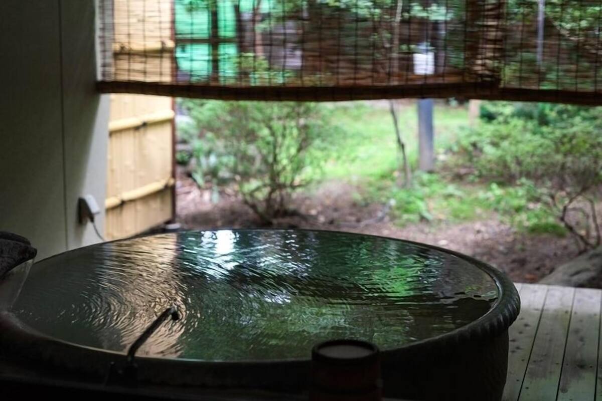 Mesa redonda com superfície refletora, uma cadeira e vista para um jardim através de uma janela com tela mosquiteira.