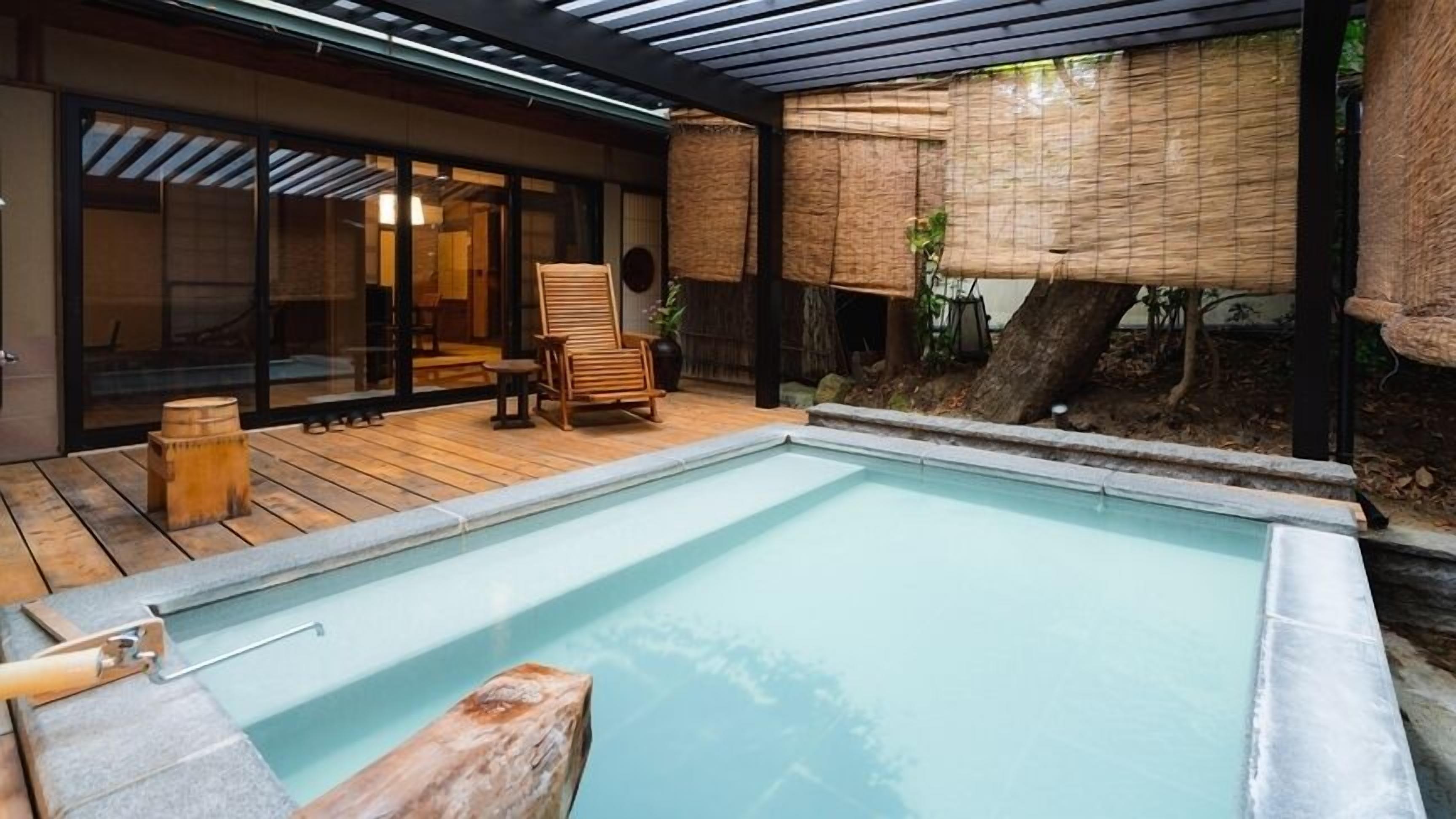 Piscina com deck de madeira, uma cadeira e uma mesa pequena.