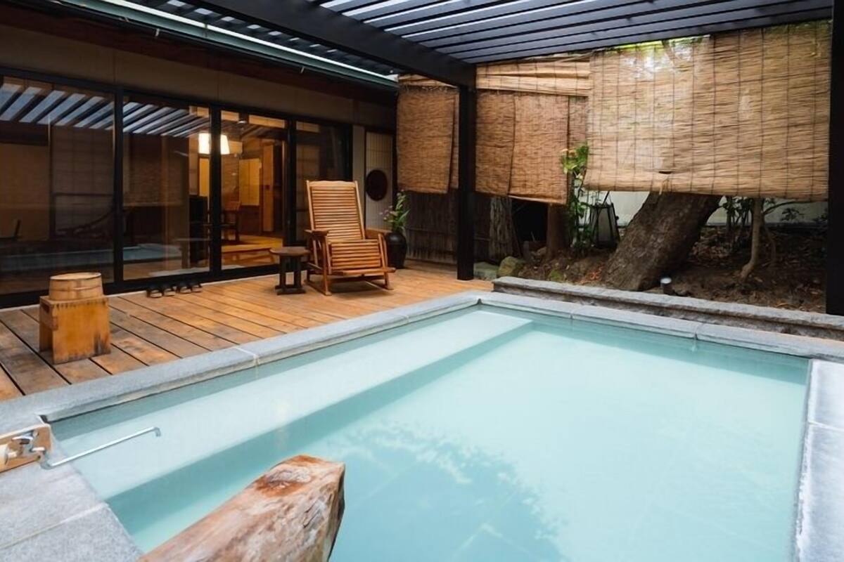 Piscina com deck de madeira, uma cadeira e uma mesa pequena.