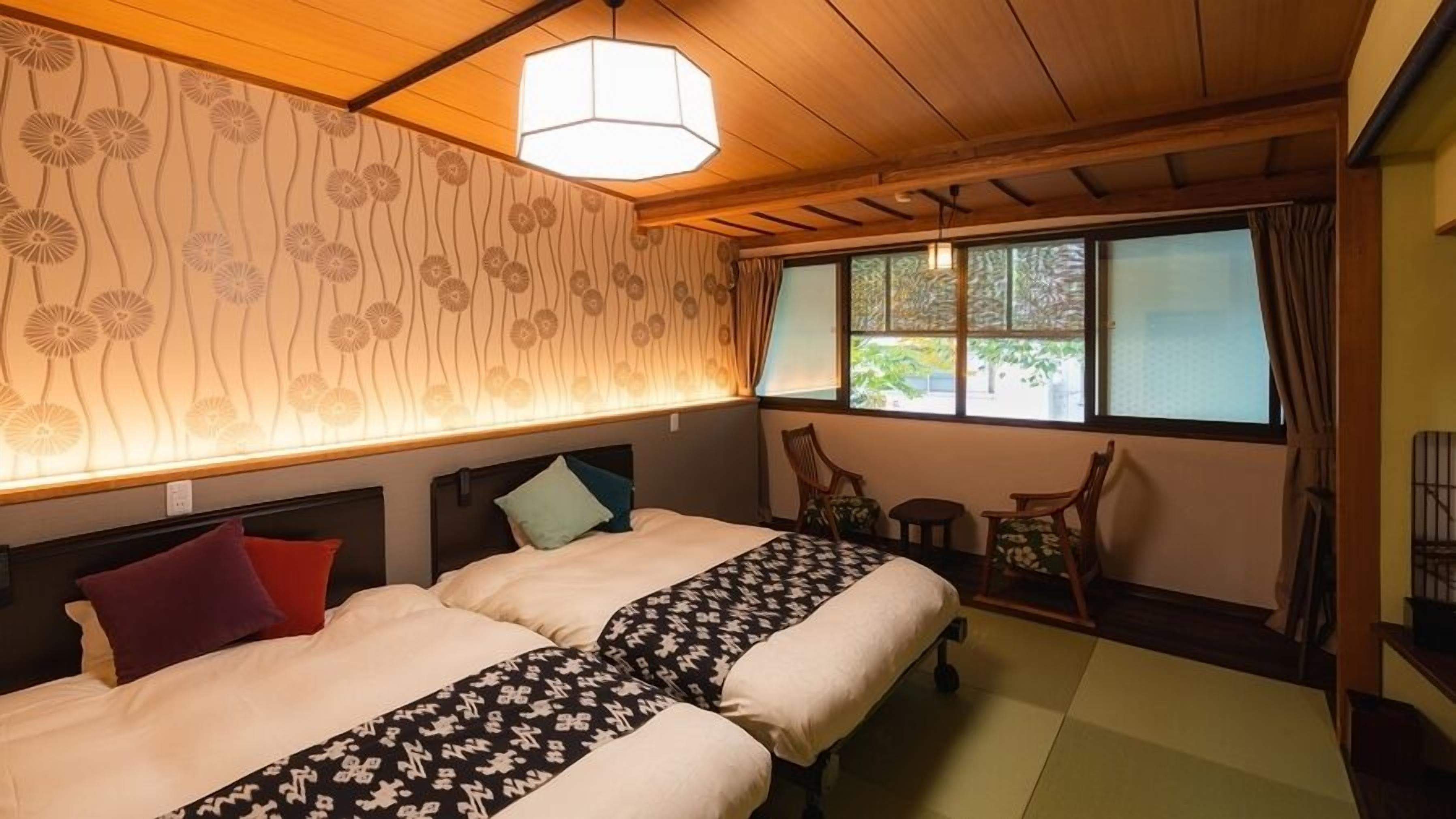 Quarto com duas camas, uma janela com cortinas, uma cadeira e parede estampada.