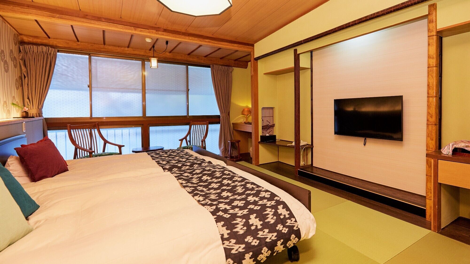 Quarto de hotel com cama, televisão, escrivaninha e janela com cortinas.