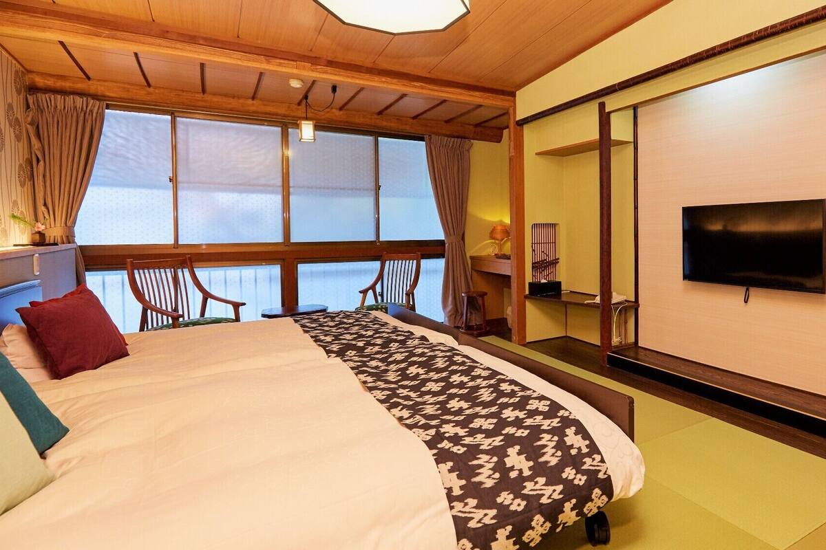 Quarto de hotel com cama, televisão, escrivaninha e janela com cortinas.