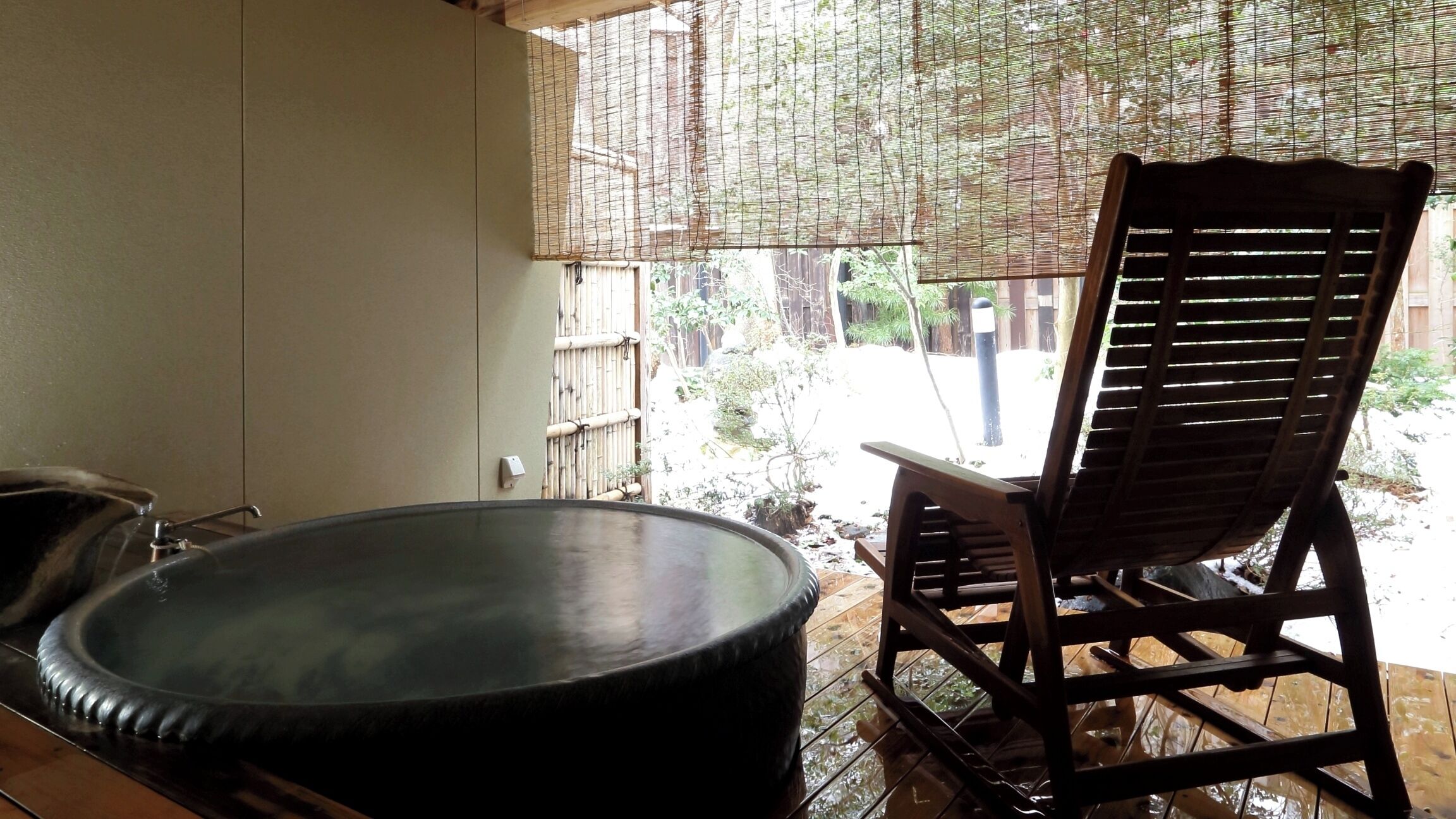 Uma banheira de hidromassagem com uma cadeira de madeira em um quarto com divisória de bambu.