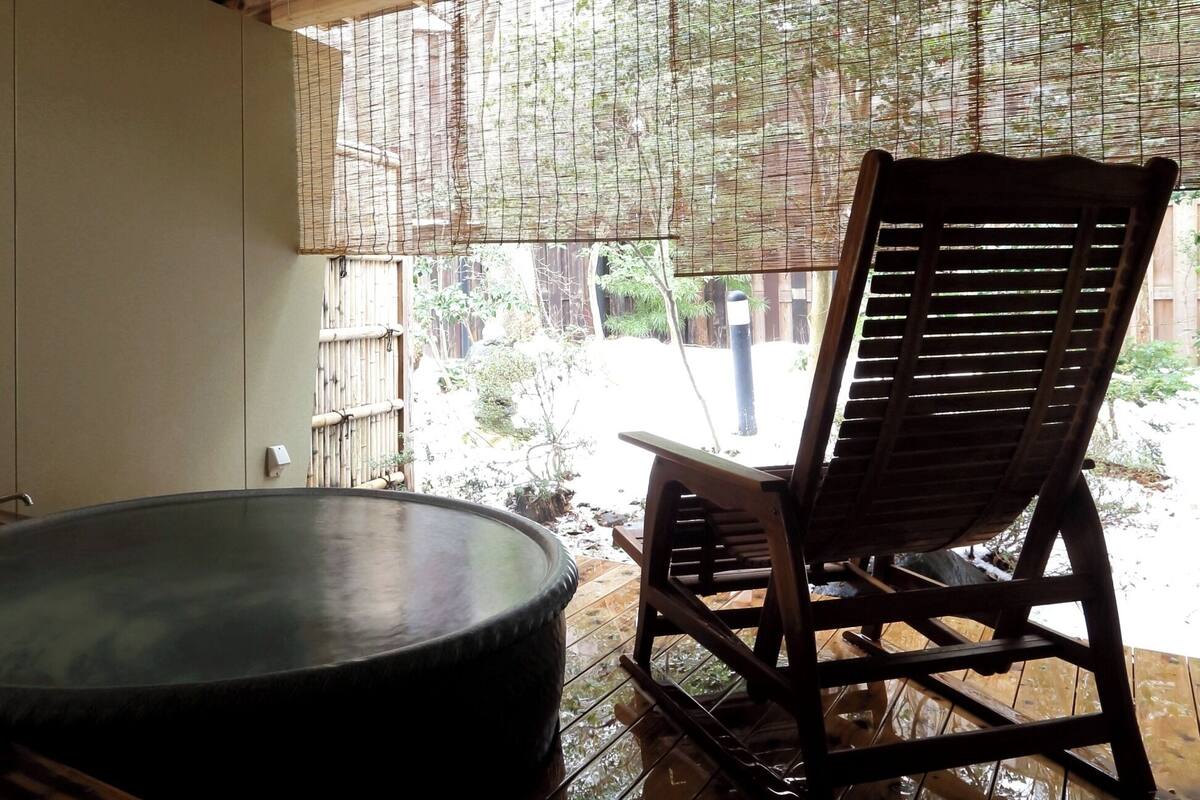 Uma banheira de hidromassagem com uma cadeira de madeira em um quarto com divisória de bambu.
