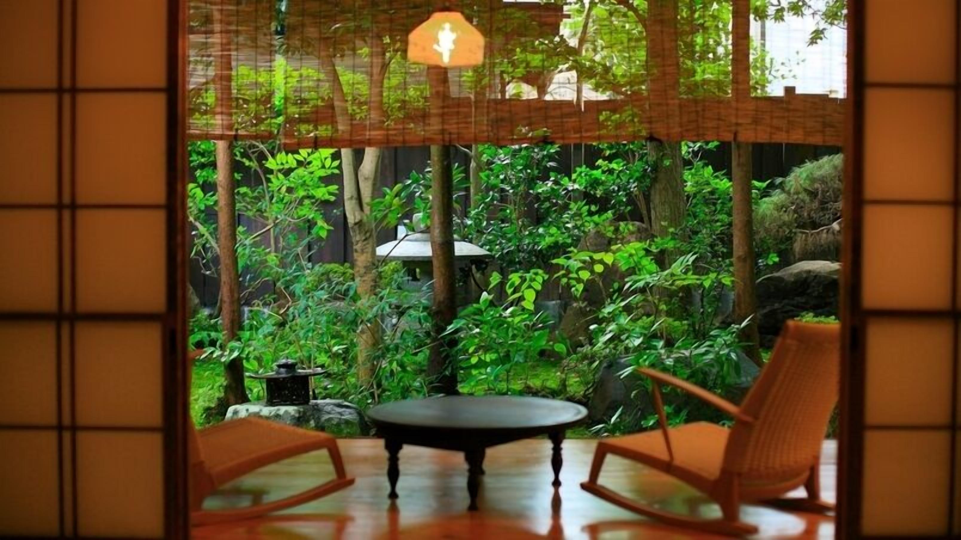 Quarto com vista para um jardim exuberante, uma mesa pequena e duas cadeiras de balanço.