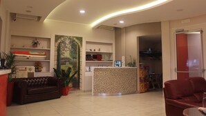Um saguão de hotel com balcão de recepção, área de estar e estantes com comodidades.