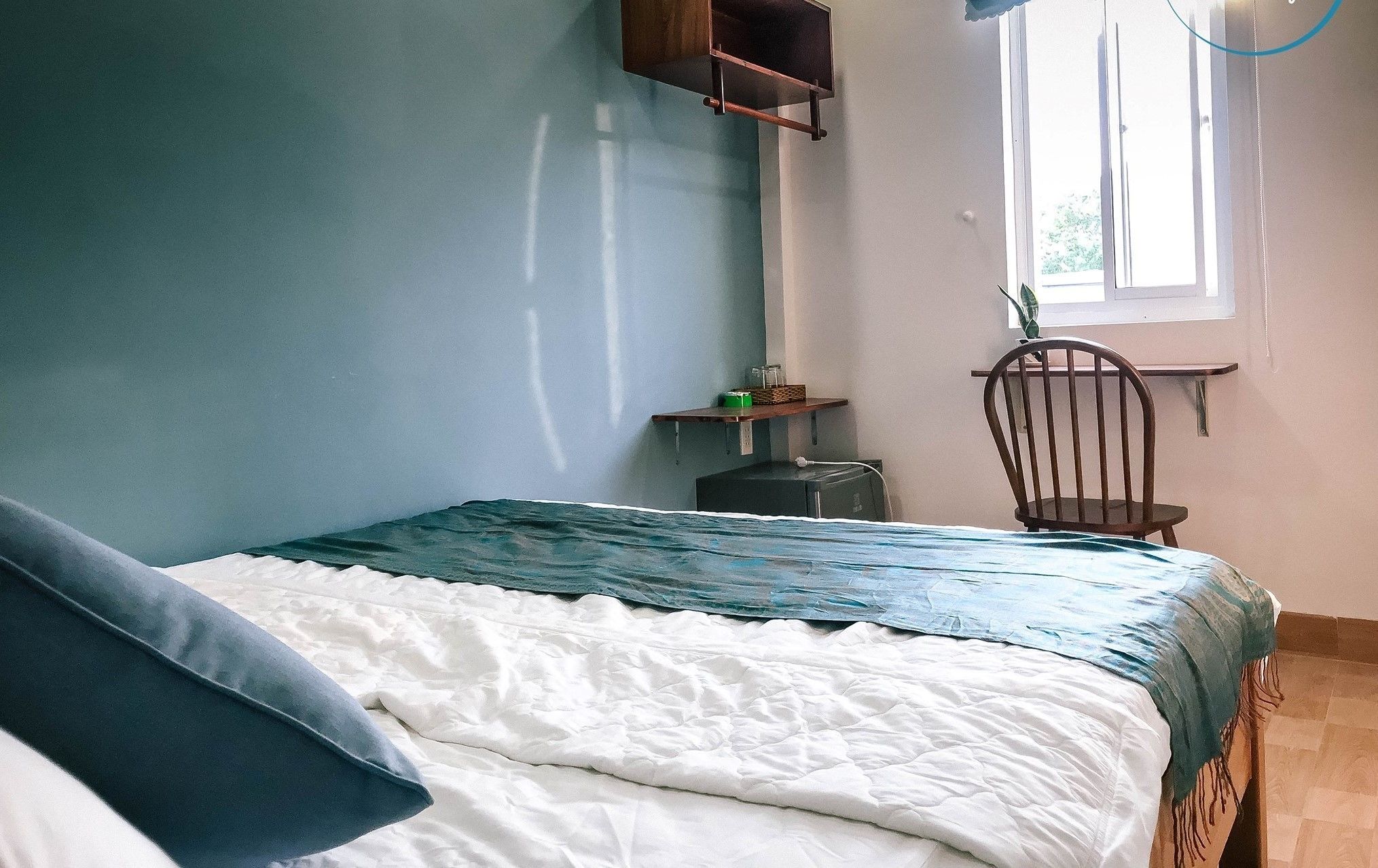 Um quarto com uma cama, uma cadeira, uma estante e uma janela.