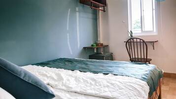 Um quarto com uma cama, uma cadeira, uma estante e uma janela.