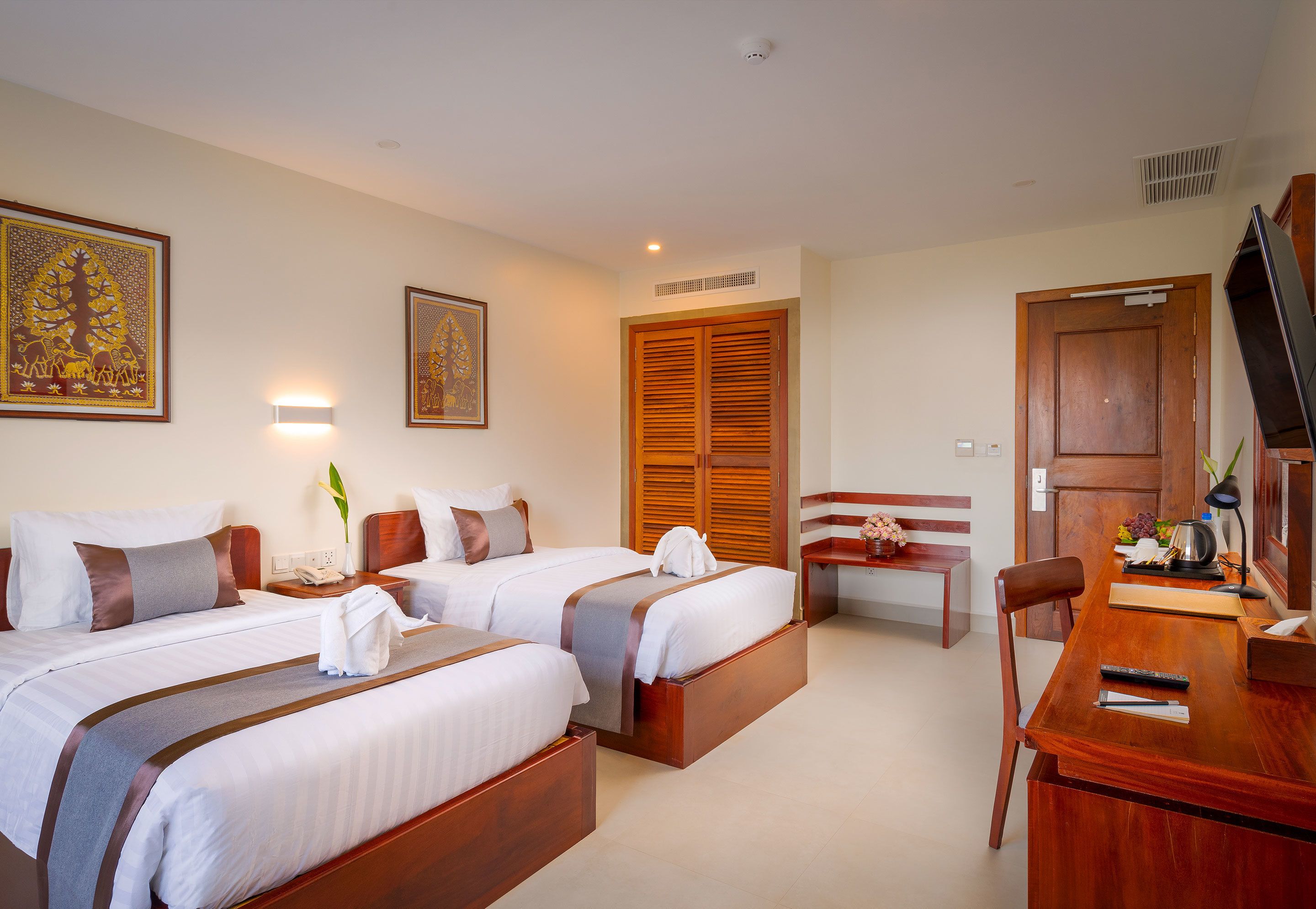 Quarto de hotel com duas camas, uma escrivaninha, uma cadeira, uma televisão e uma porta.