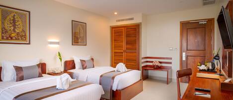 Quarto de hotel com duas camas, uma escrivaninha, uma cadeira, uma televisão e uma porta.