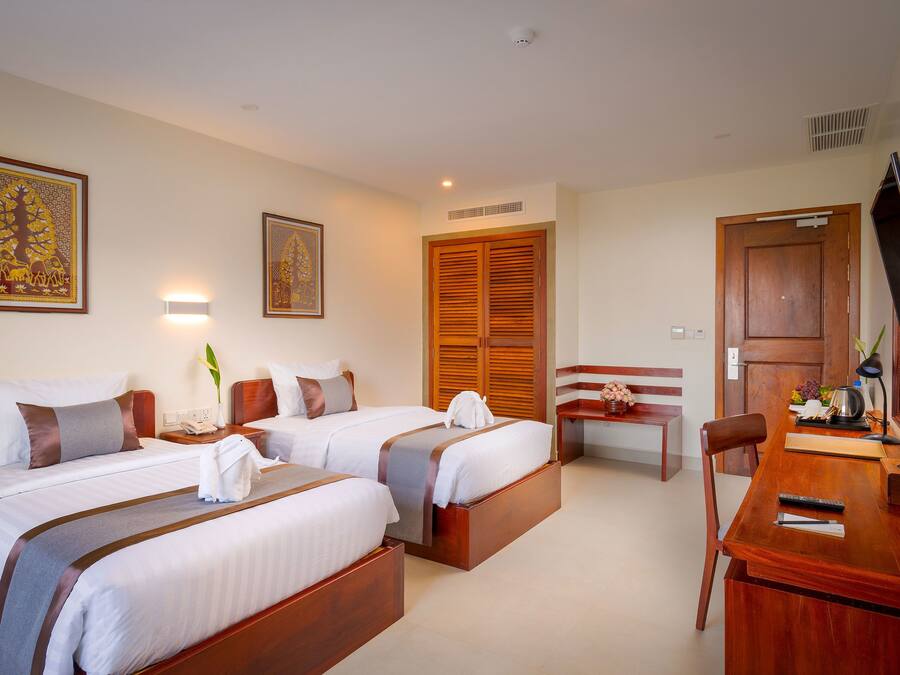 Quarto de hotel com duas camas, uma escrivaninha, uma cadeira, uma televisão e uma porta.