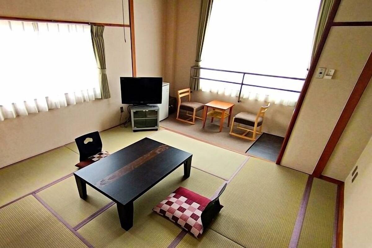 Quarto japonês tradicional com tatames, uma mesa baixa, uma televisão e uma porta deslizante.