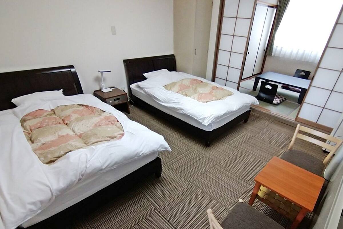 Quarto de hotel com duas camas, uma escrivaninha e uma cadeira.